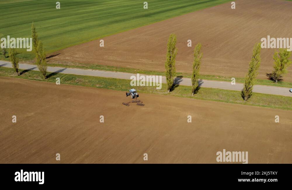 Cinematic aerial view on tractor with disc harrow in field near asphalt ...