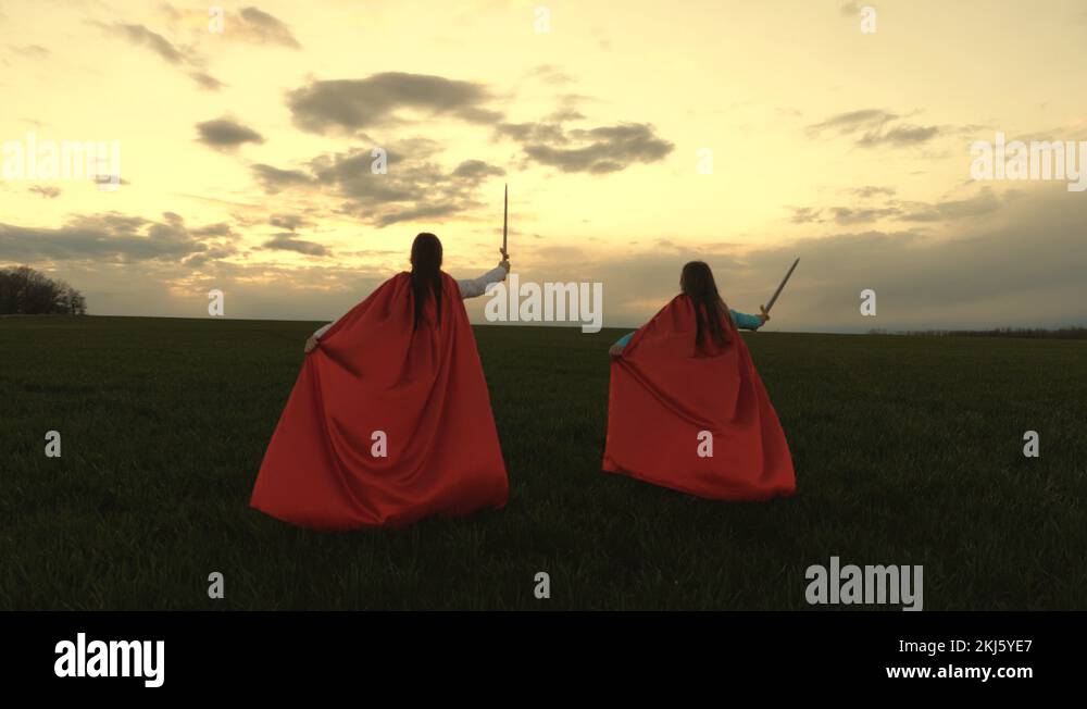 girls in red cloaks run with swords in hand across field playing ...