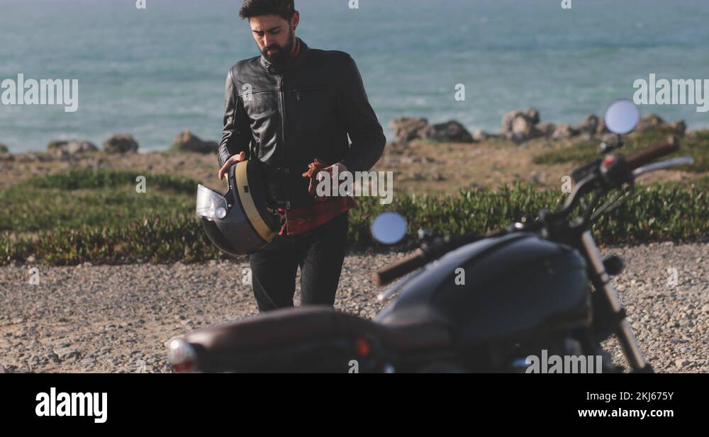 Handsome biker man walking from seafront getting on classic motorcycle ...