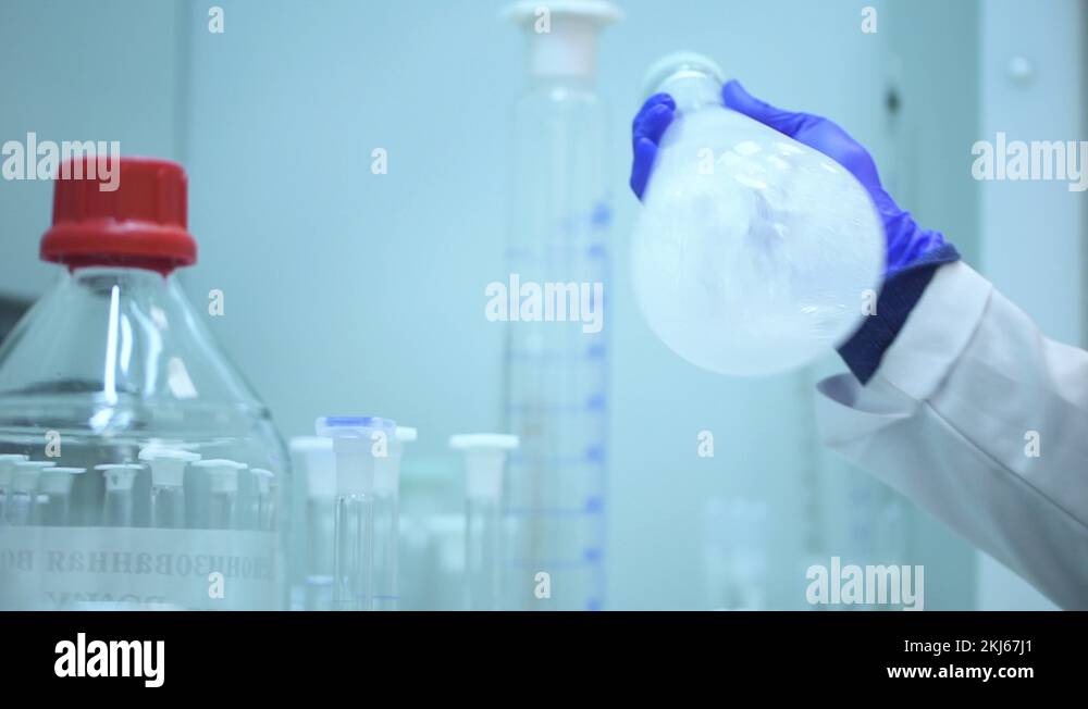 chemist in chemical laboratory holding a flask transparent liquid ...