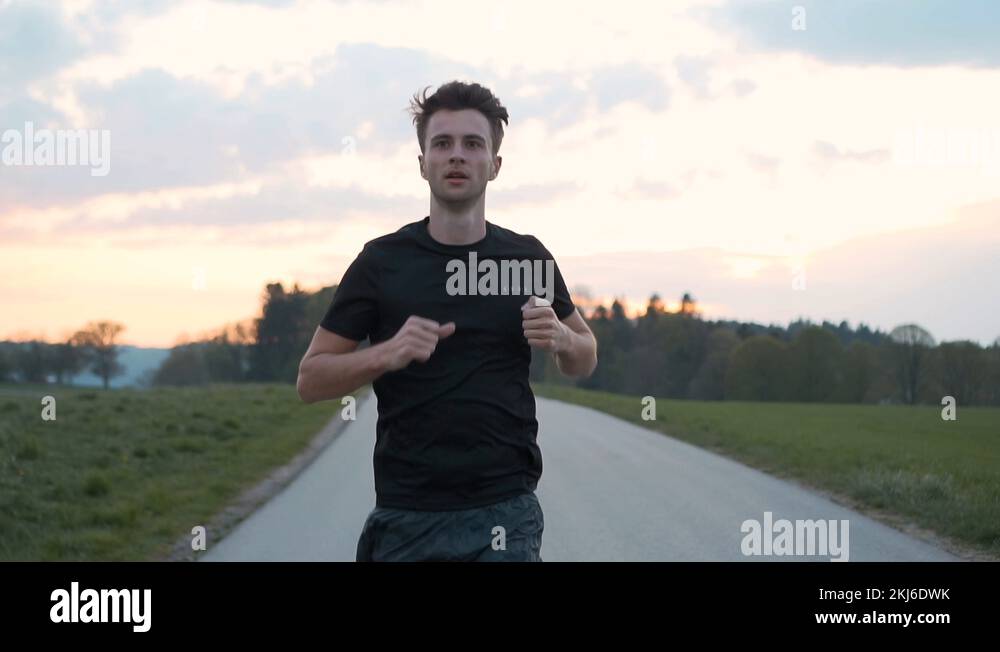 Front dolly of man athlete running on street between meadows, slow ...