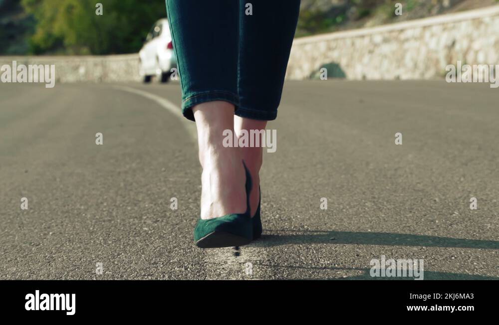 Female legs in high heels go along the road along a white dividing line ...