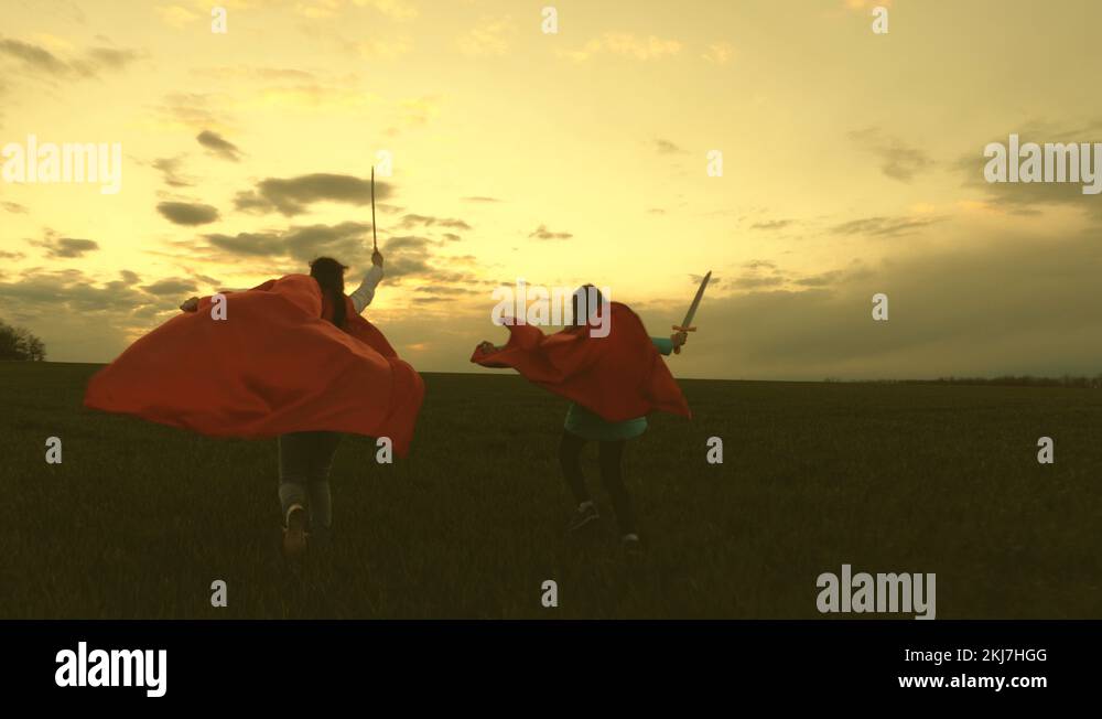 girls in red cloaks run with swords in hand across field playing ...