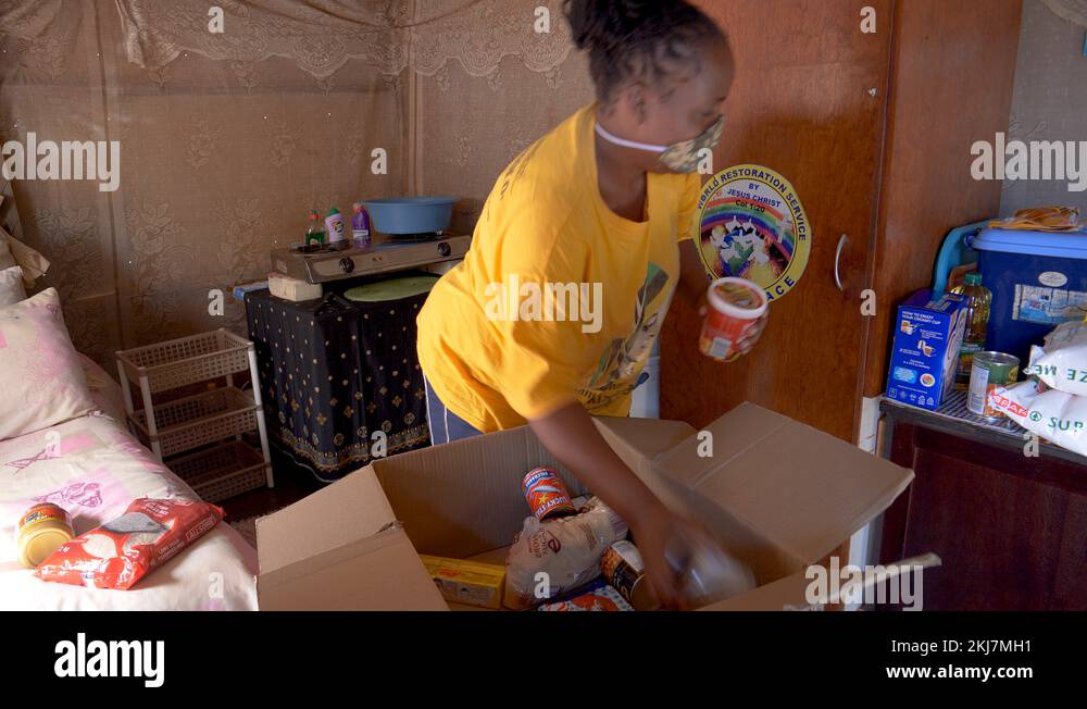 Black African woman unpacks a food parcel in squatter camp that was ...