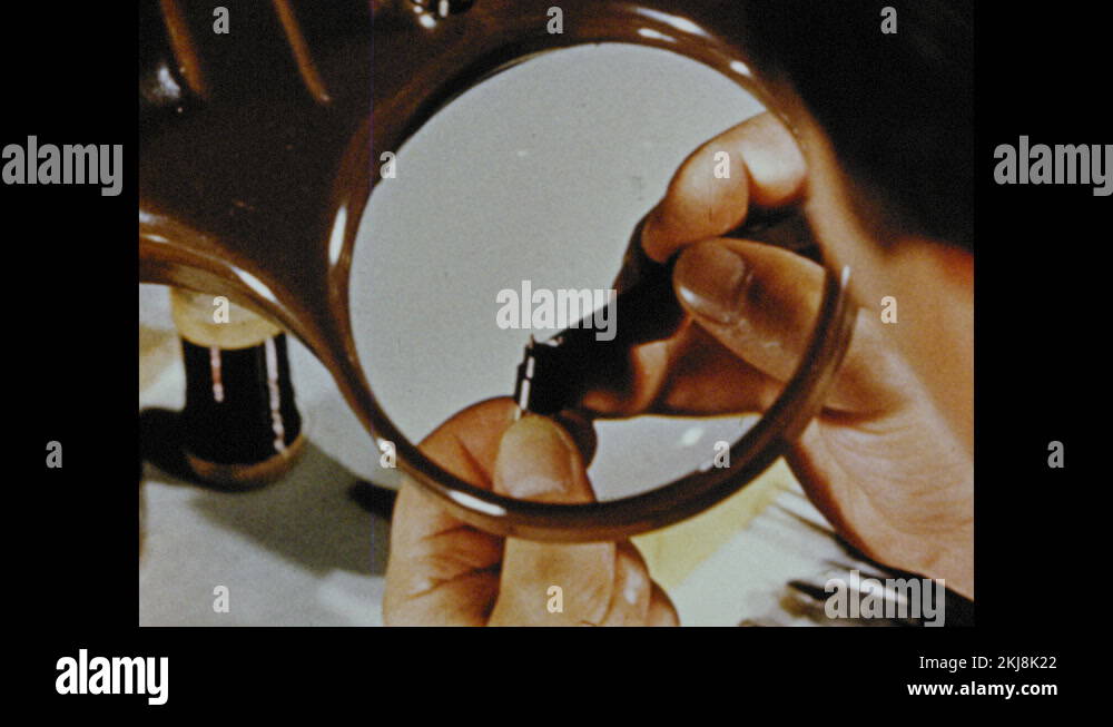 1950s: View through magnifying glass, hands assembling transistor. Man ...