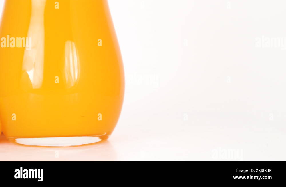 Glass jug with fresh orange juice spinning fast on left side of white ...