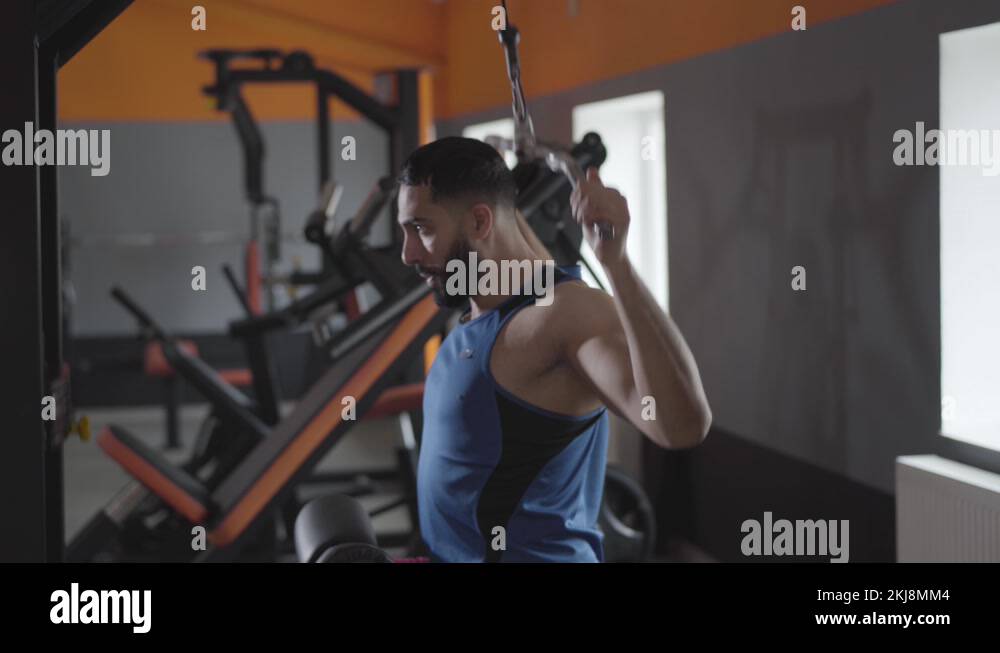 Side view of muscular Middle Eastern sportsman using shoulder pull down ...