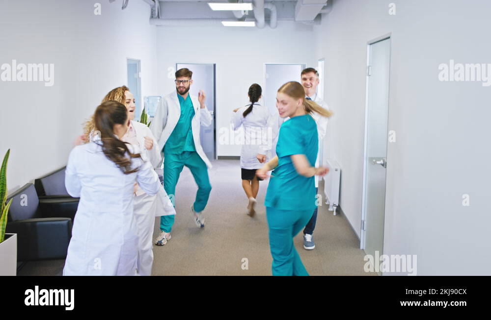 In a modern hospital corridor group of doctors and nurses dancing ...