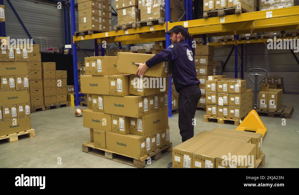 Male warehouse employee moving cardboard boxes from one pallet to the ...