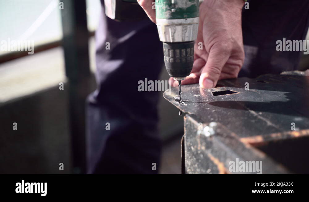 Man using electric hand drill for boring holes in thin black metal ...