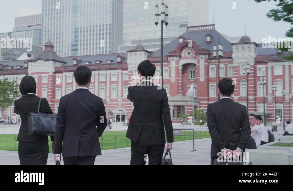 four young japanese business people in suits walking in front of Tokyo ...
