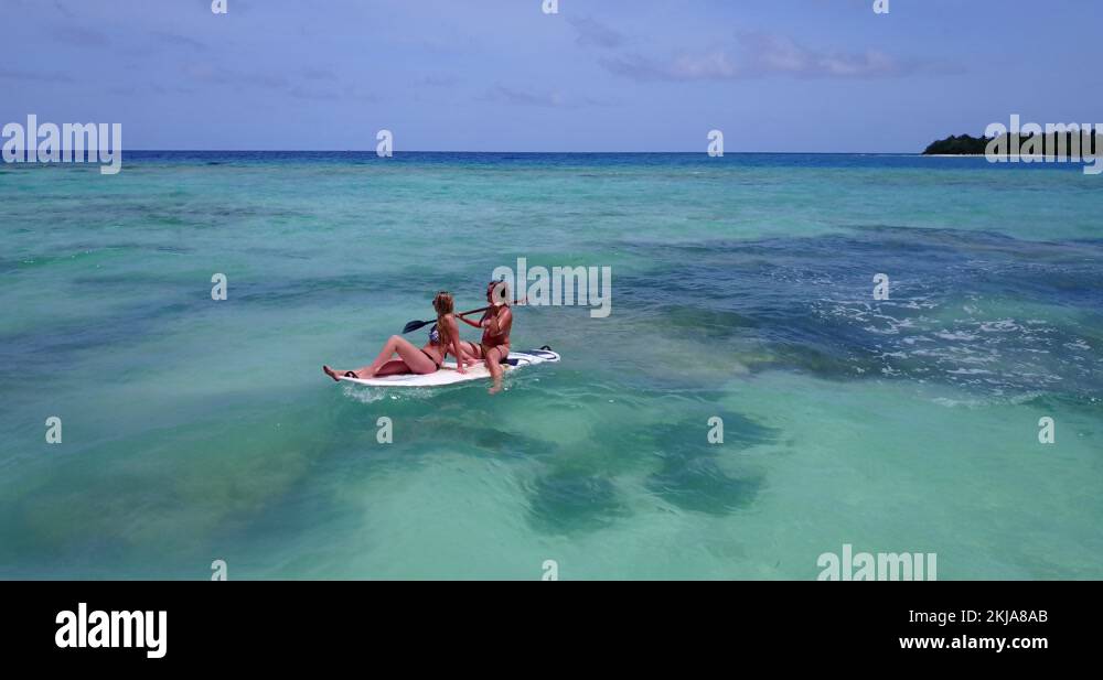 Two girls paddling and sunbathing on top of a surfboard floating above ...