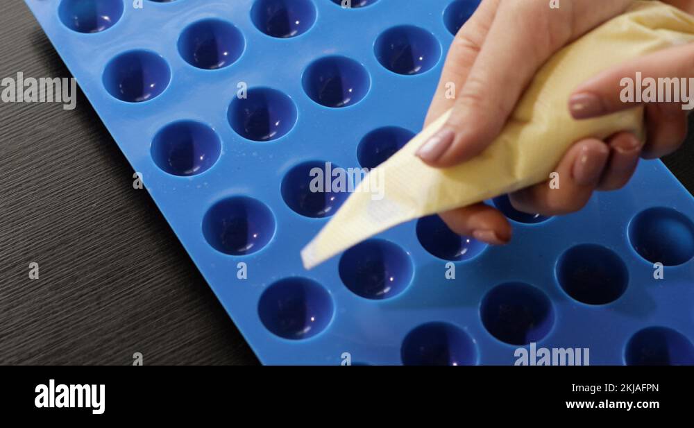 Baker's hands pouring liquid white chocolate in form mold from pastry ...
