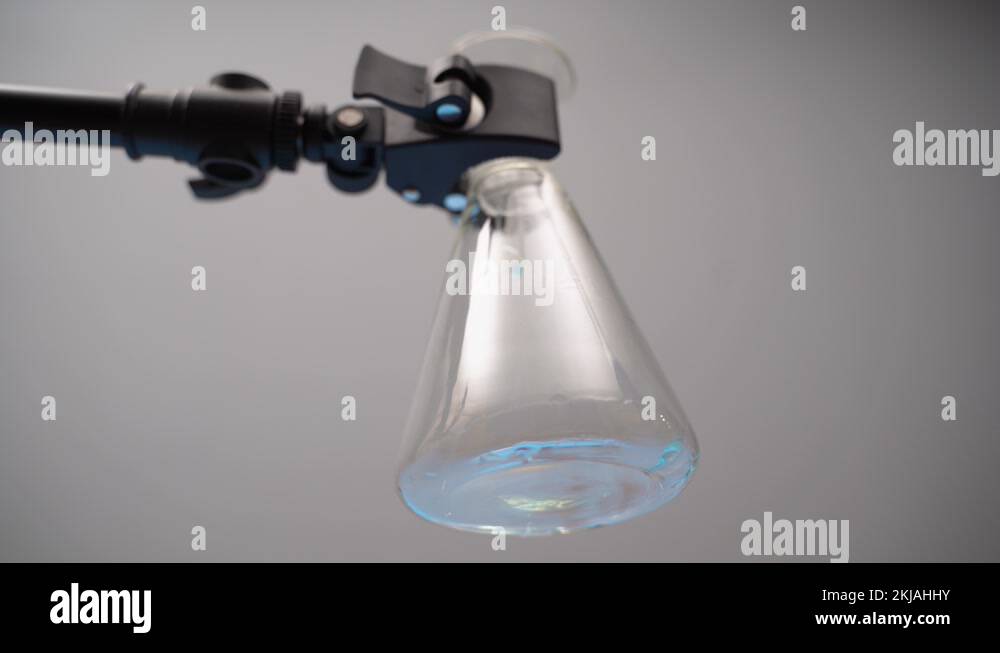 Blue liquid poured in a glass flask. Liquid flows into a Erlenmeyer ...