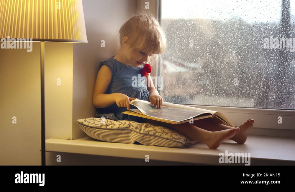Cute baby girl reading book on window sill at home Stock Video Footage ...