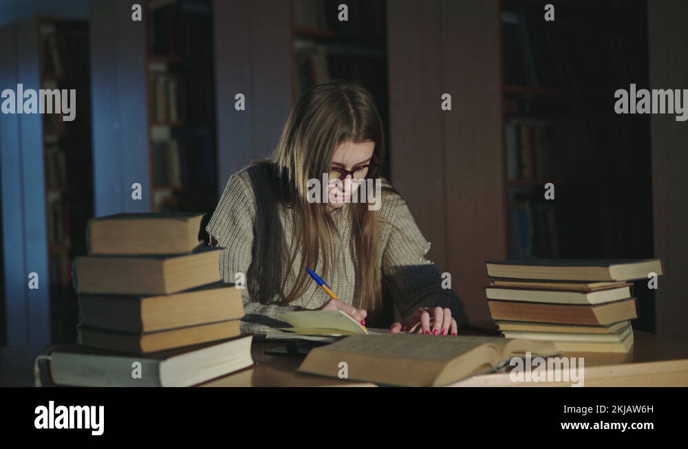 Girl noting compendium from books at a desk and gazing into it in half ...