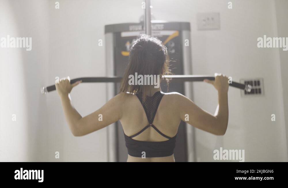 Backside of fitness girl working out at gym using lat pulldown ...