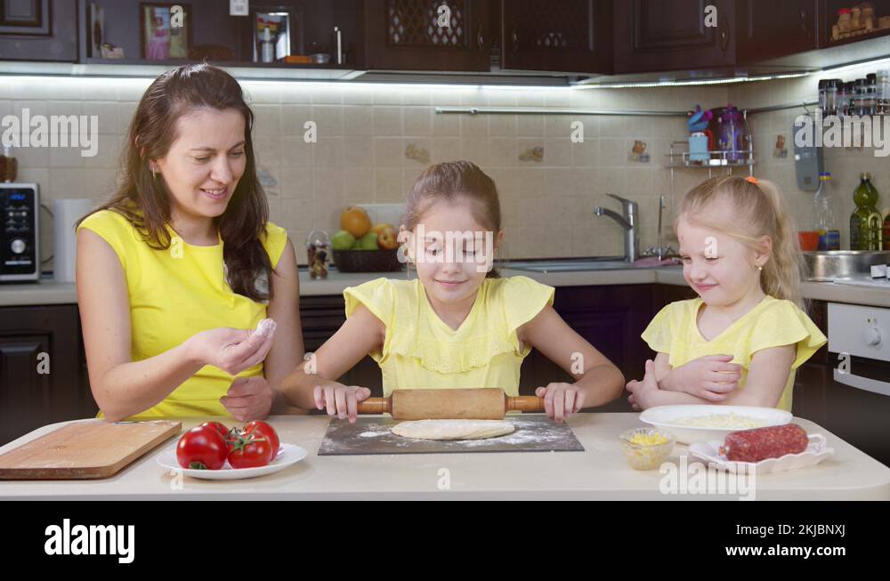 Mom and children cook in the kitchen. Little girl smooths pizza dough ...
