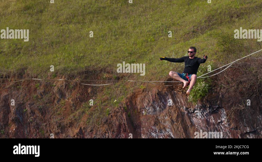 Slacklining, a man is sitting on a rope stretched over a massive pit ...