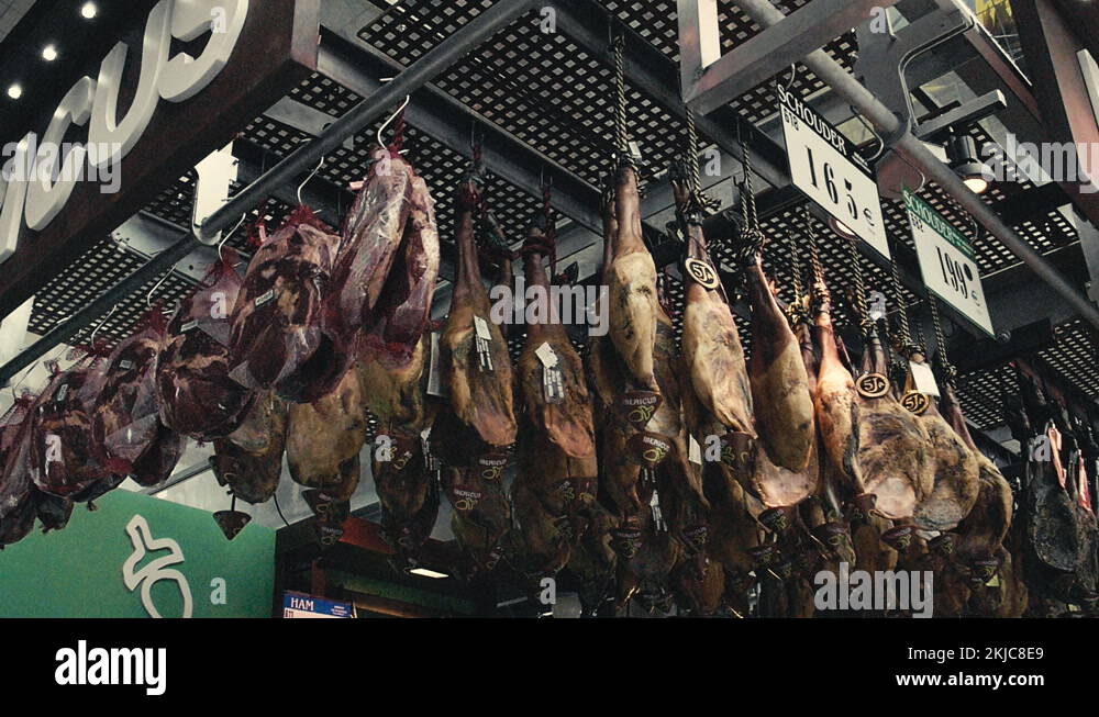Legs of cured iberico meats hanging on the ceiling inside market hall ...