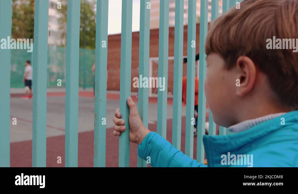 A sad little boy watching another kids playing football behind the ...