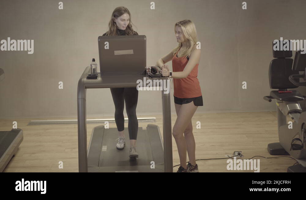Blond personal trainer adjusting speed on treadmill and talking to ...