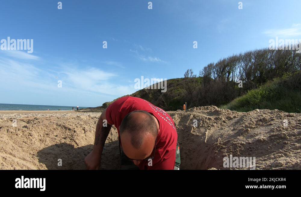 A Man Digging A Hole On The Beach Sand In Brittas Bay Using A Shovel In ...