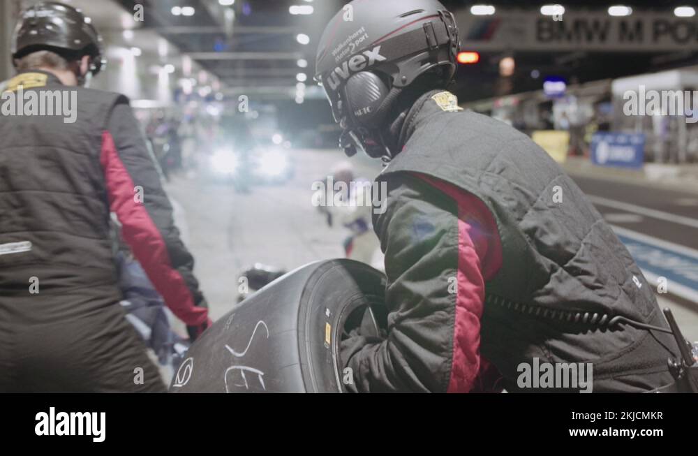 Pit crew mechanic changing slick tire on a BMW race car at night in the ...