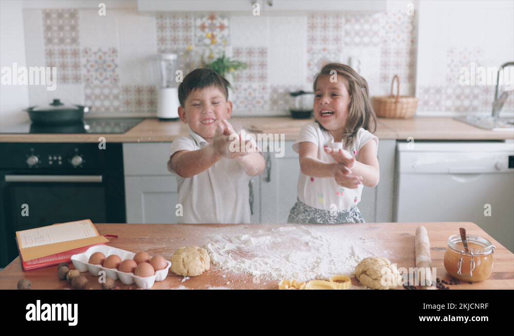 Funny kids cooking together. Girl and boy is beating the dough ...