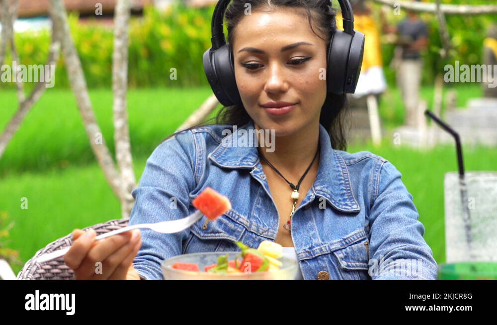 Young beautiful asian woman listen to music, eat fruit salad in cafe ...