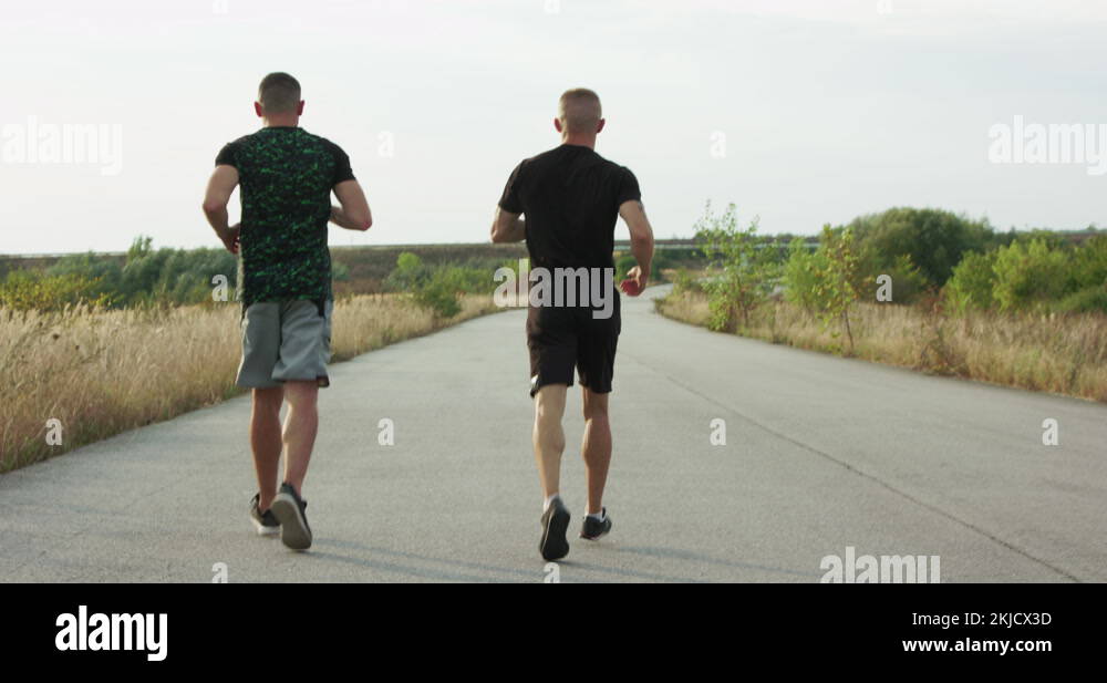 Back view of two sportsmen jogging on a path synchronously among nature ...