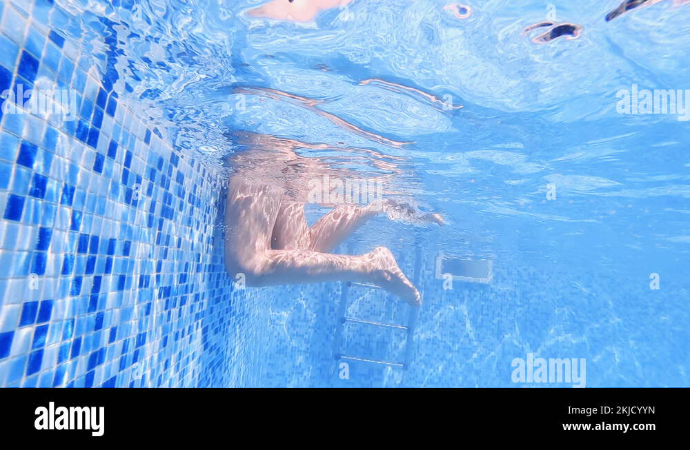 Girl by the edge of the pool splashing water with her feet, underwater ...
