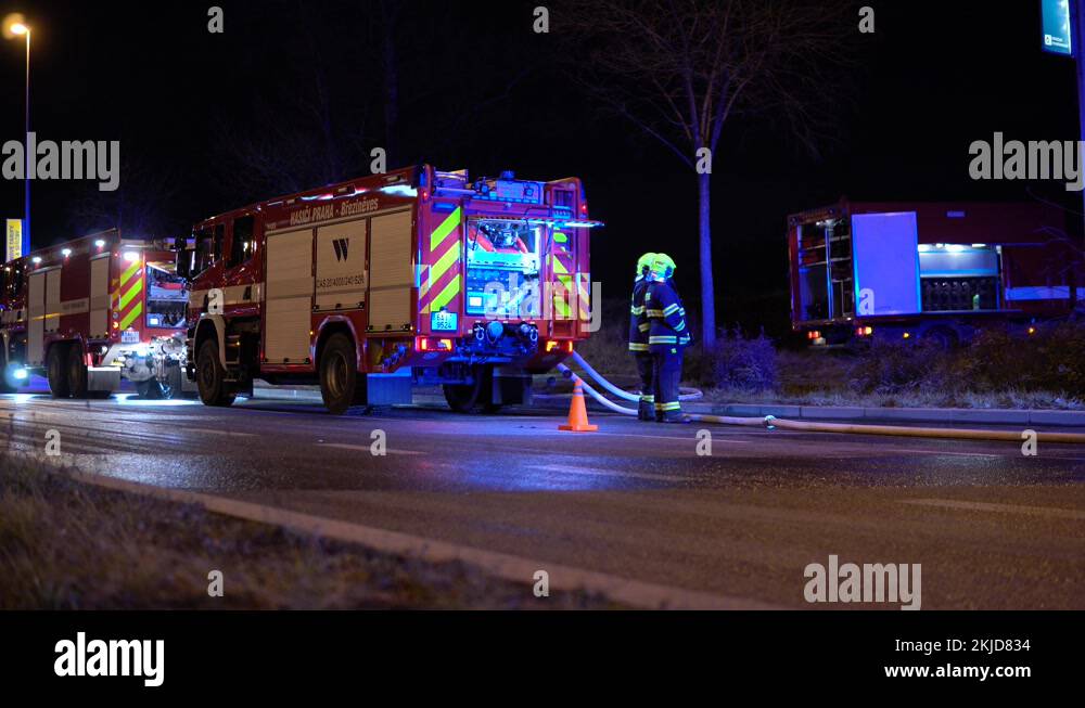 Two firefighters stand by fire trucks and watch a situation off the ...