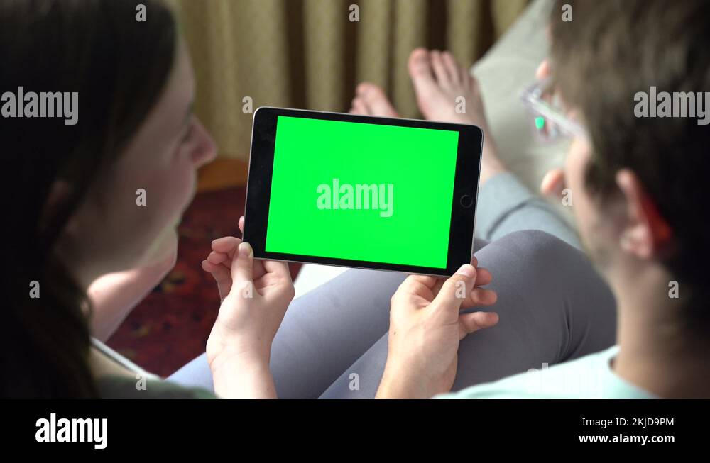 Young teen girl and man hold a tablet with green screen on it and wave ...