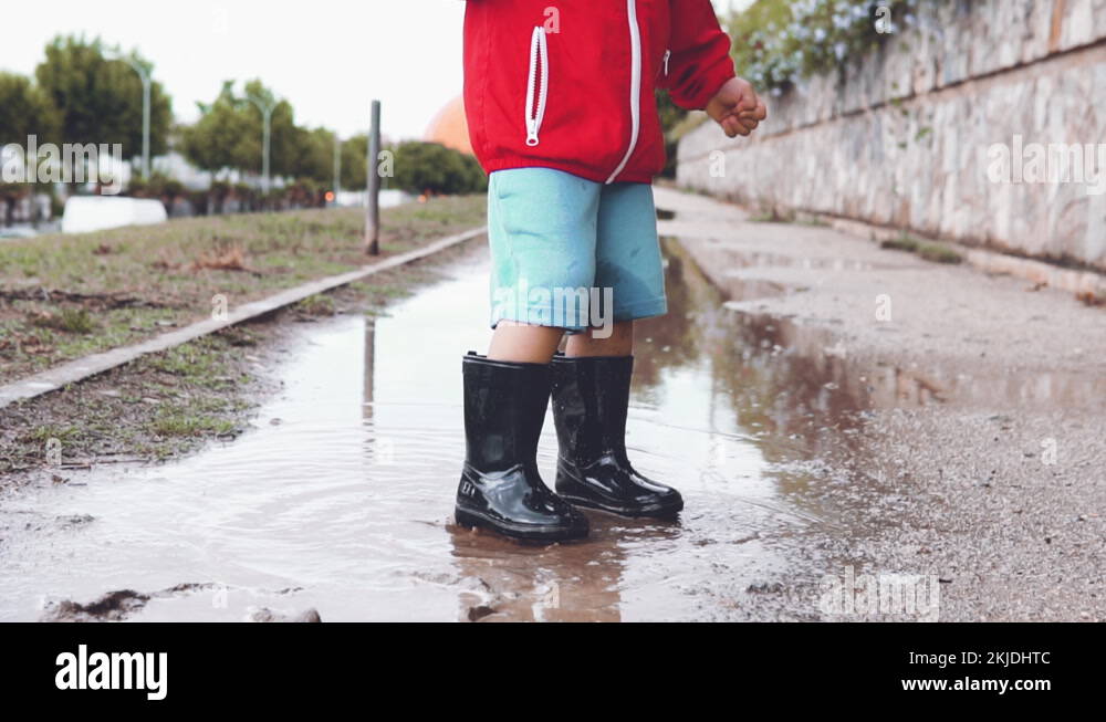 Little boy wearing rubber boots splashing water from a puddle to the ...