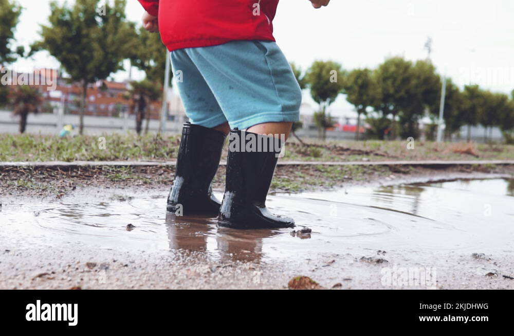 Kid wearing rubber boots jumping in a puddle in slow motion. Child ...