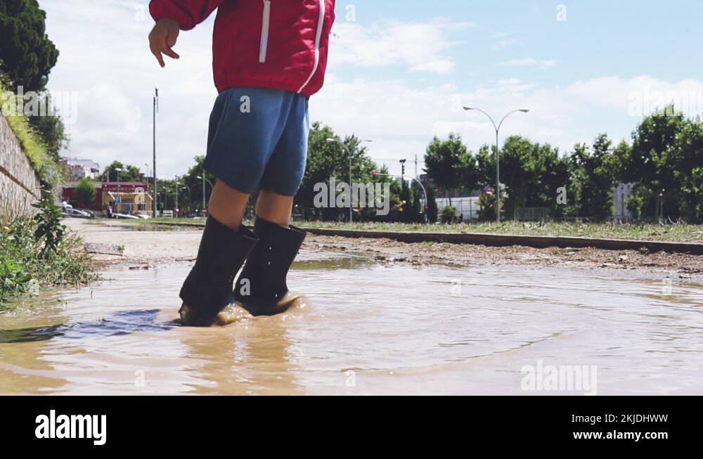 Kid jumping repeatedly in a muddy puddle puddly splashing water in slow ...