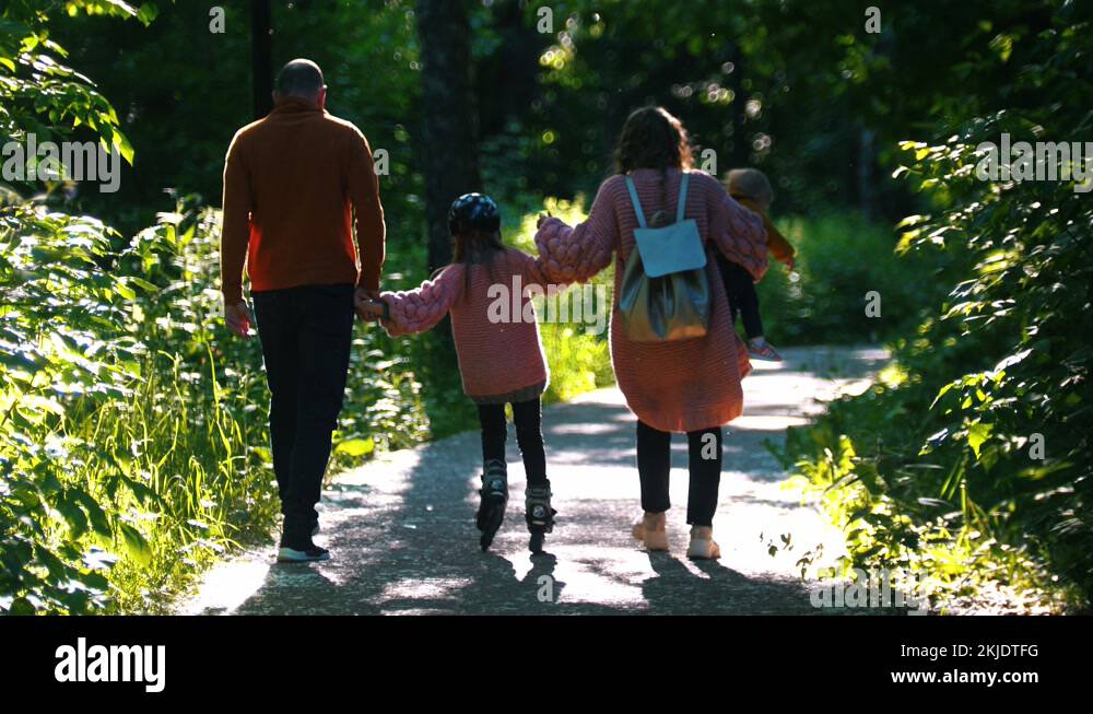 Young family of parents and two little kids walking in the summer park ...
