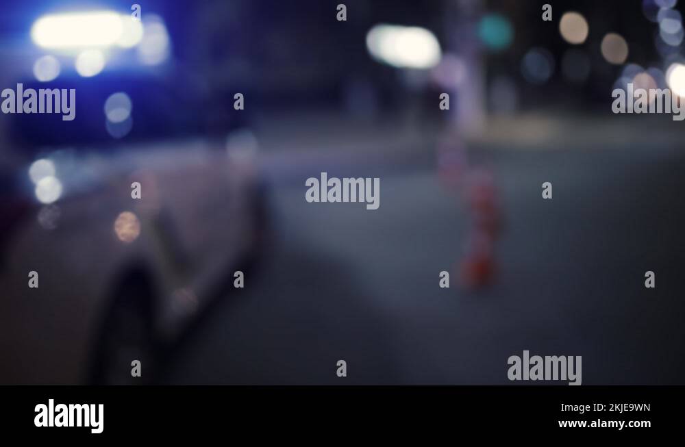 Unfocused shot of police car with sirens and traffic cones on city road ...