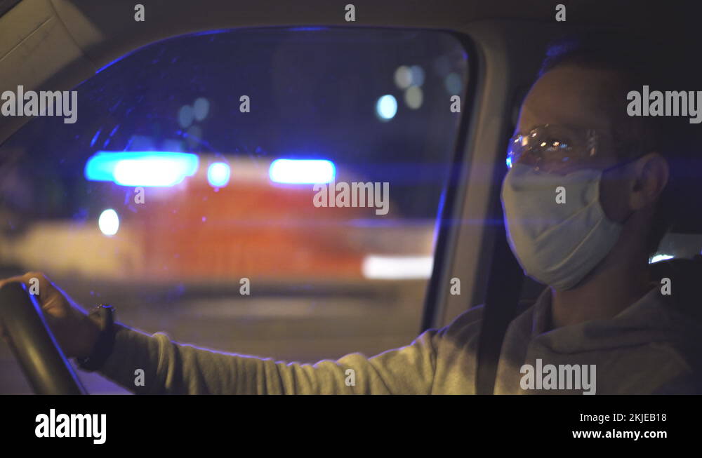 The man with a face mask and protective glasses driving a car on the ...