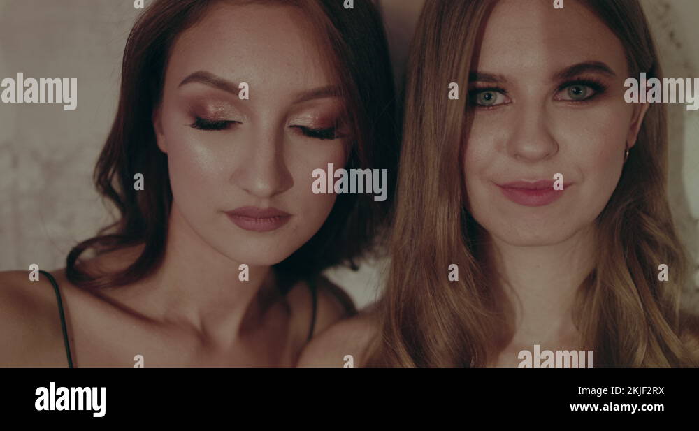 Two pretty contrast girls open, close eyes and look into camera with ...
