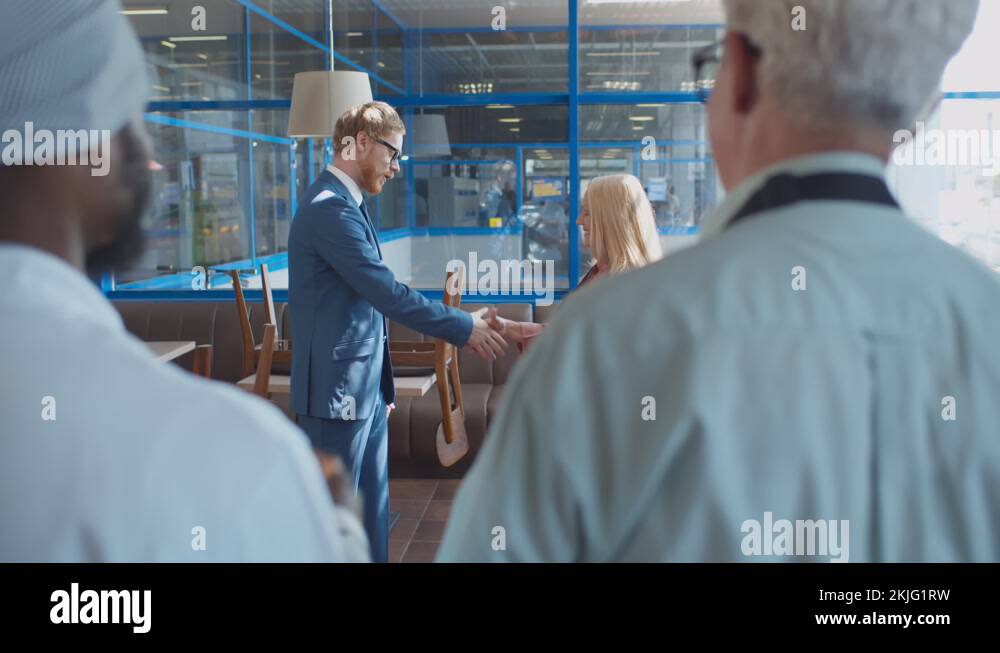 Back view of cafe staff watching young manager welcoming new employee ...