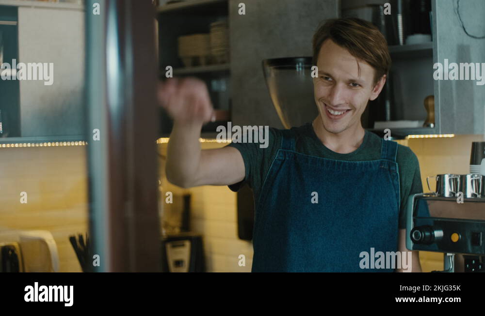 Friendly coffee shop owner invites new guests waving hand to costumers ...