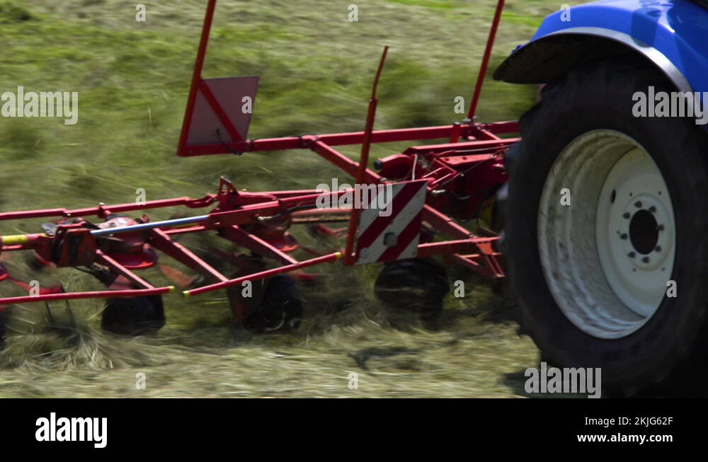 Haying equipment behind farmer tractor turning grass in drying process ...