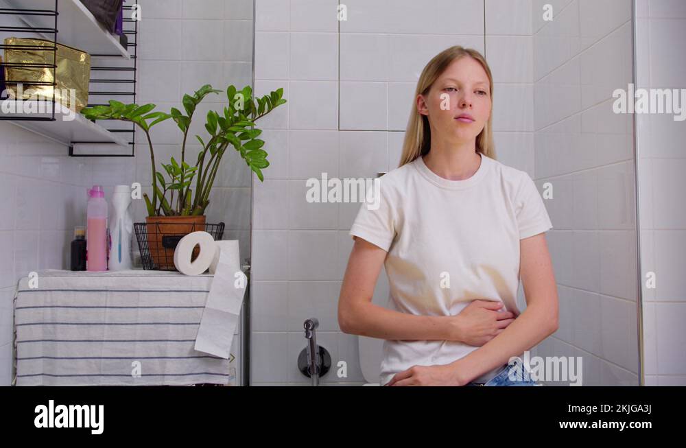 Young woman sitting on toilet holding sick stomach. Turns stomach ...