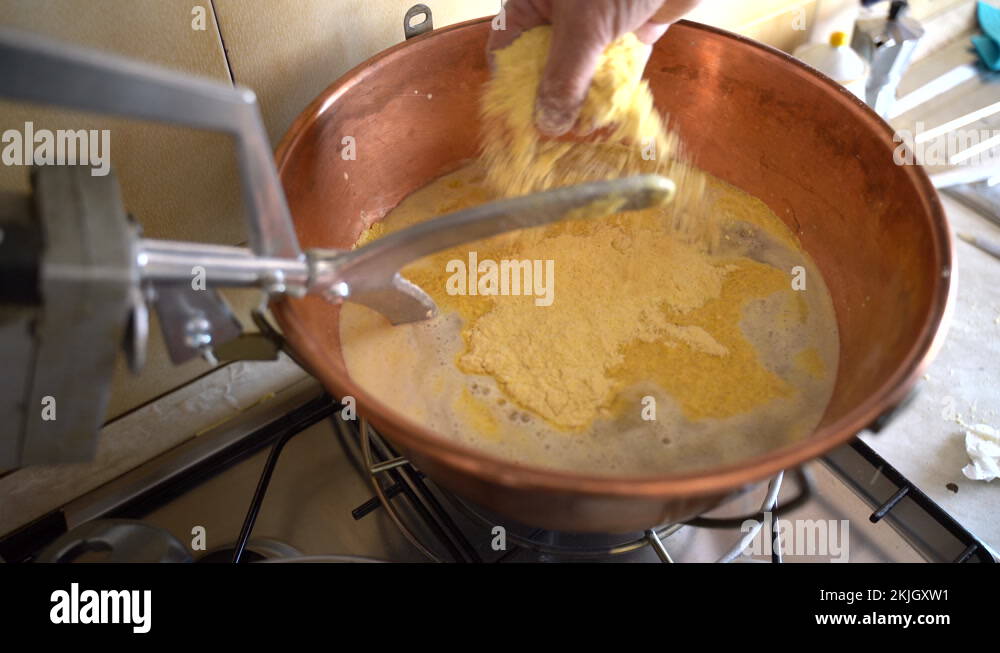 Yellow corn flour pouring in boiling water in typical copper cauldron ...