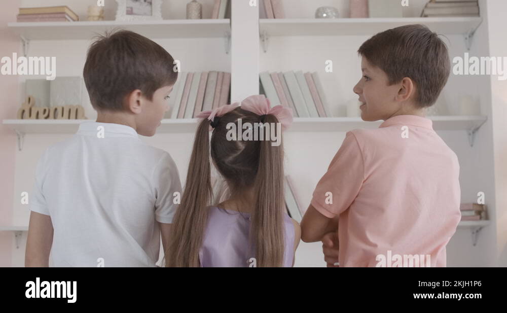 Back view of three children pointing at bookshelves and talking. Little ...