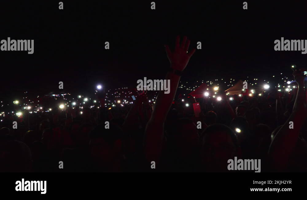 Dark background with concert crowd waving hands with mobile phone ...
