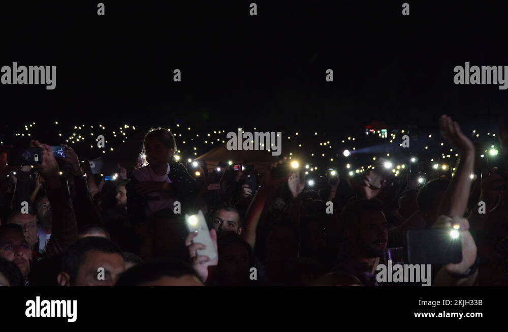 Dark background with concert crowd waving hands with mobile phone ...