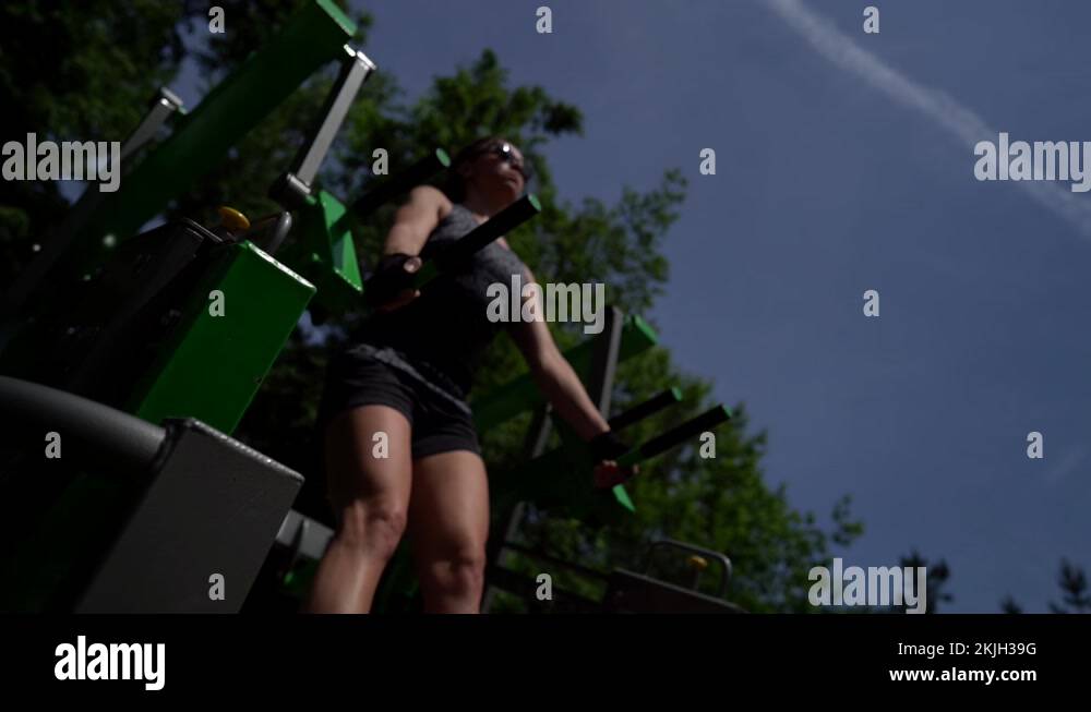 bodybuilder woman is lifting weights in open sporty area, using sport ...